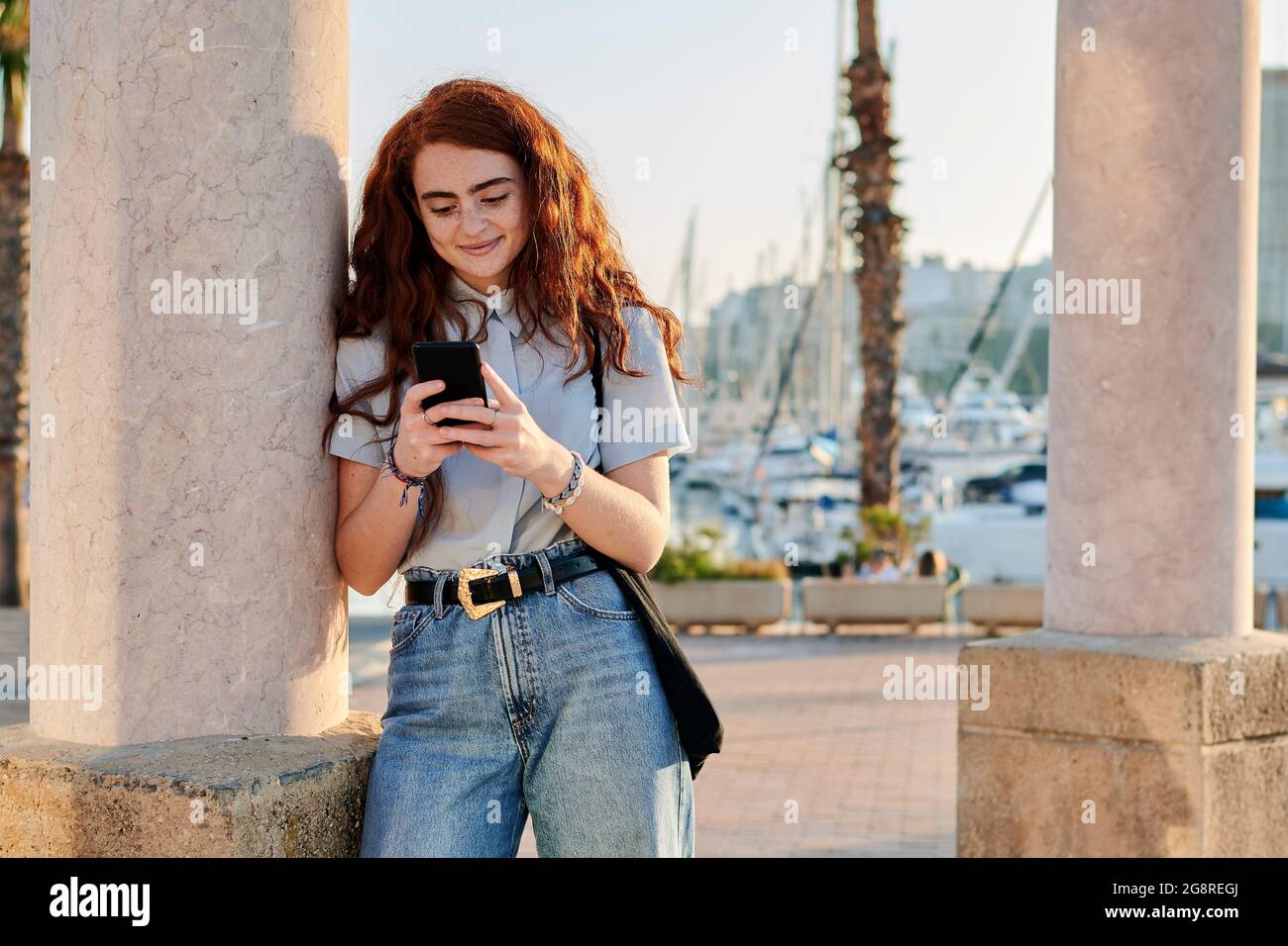 Young redhead woman looks at her mobile in a seaport Stock Photo - Alamy