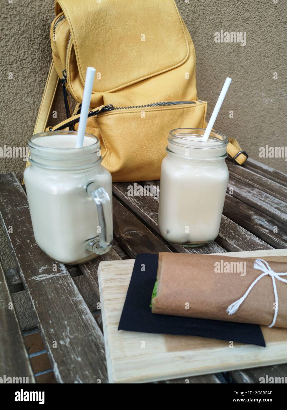 Two cups of cold latte and burrito, yellow backpack at table Stock ...