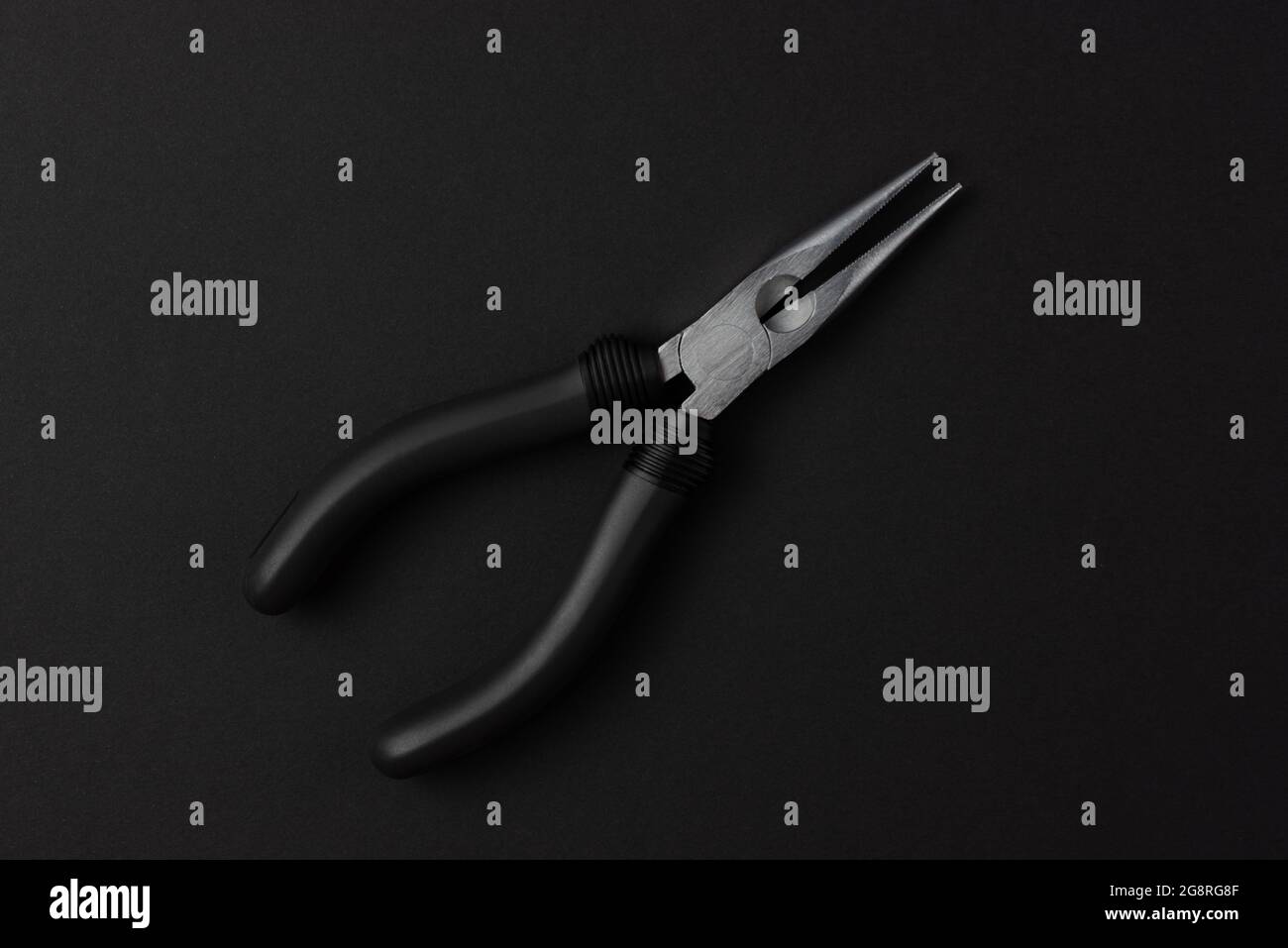 Isolated metal pliers with plastic black handles on a black background ...