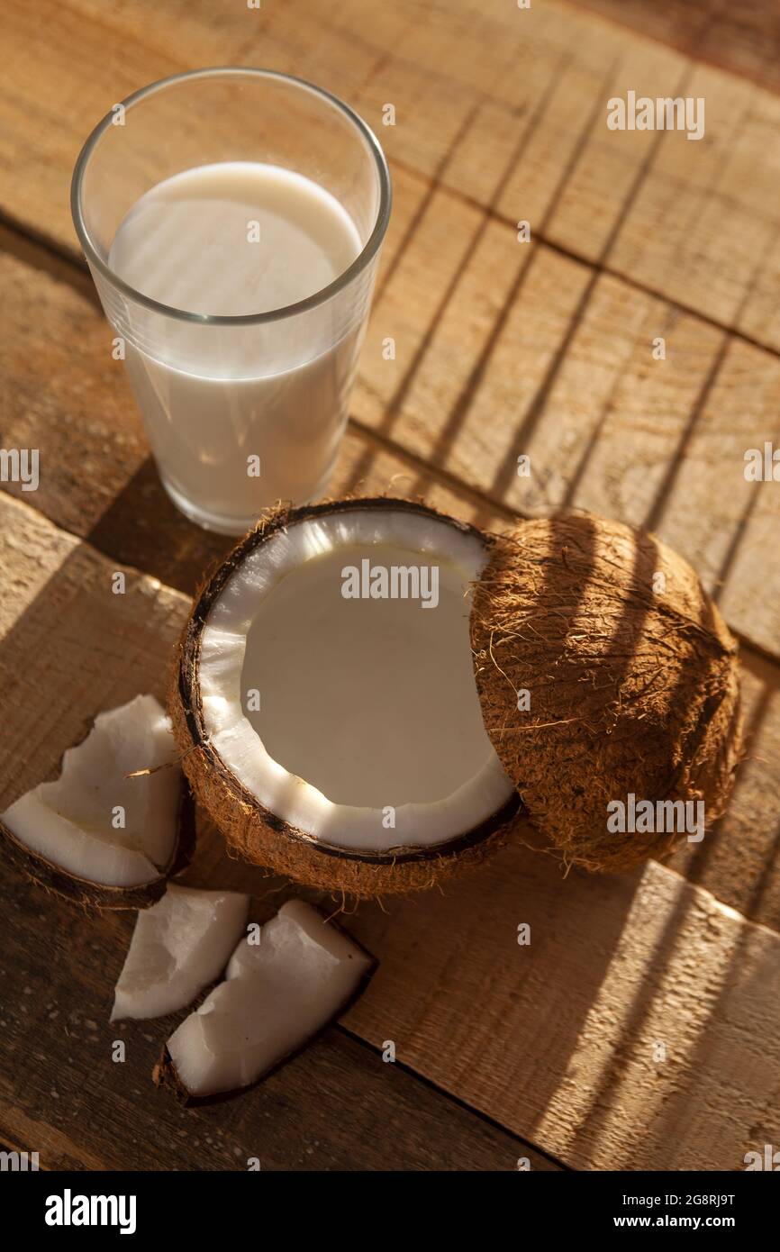 Vertical shot of fresh coconut and a glass of coconut milk on a wooden ...