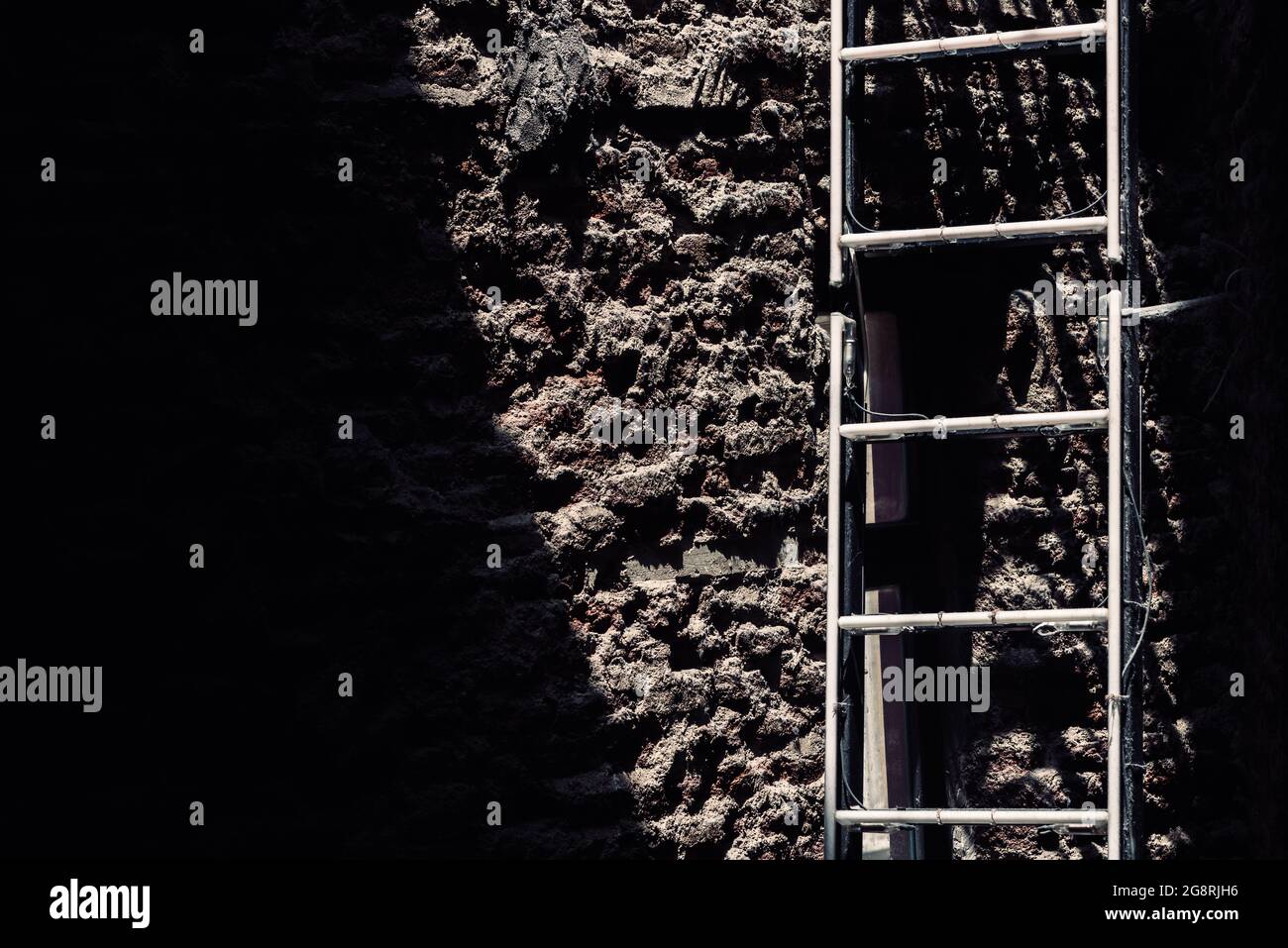 Closeup of a ladder leaned up against a rocky wall with a bright ...