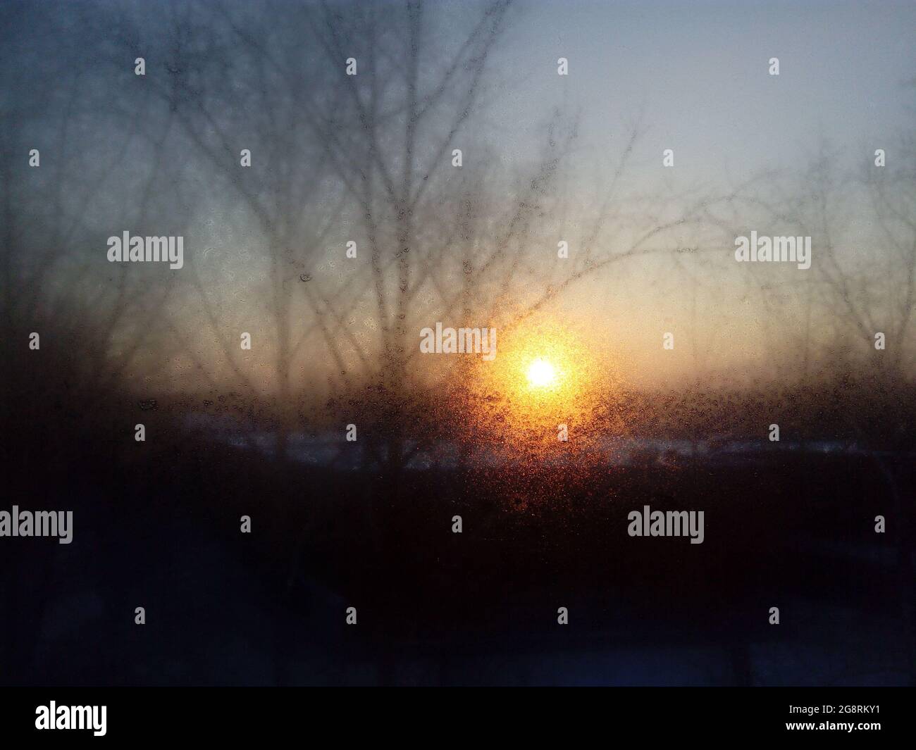 Early frosty spring morning through the foggy frosty window. Sunset ...