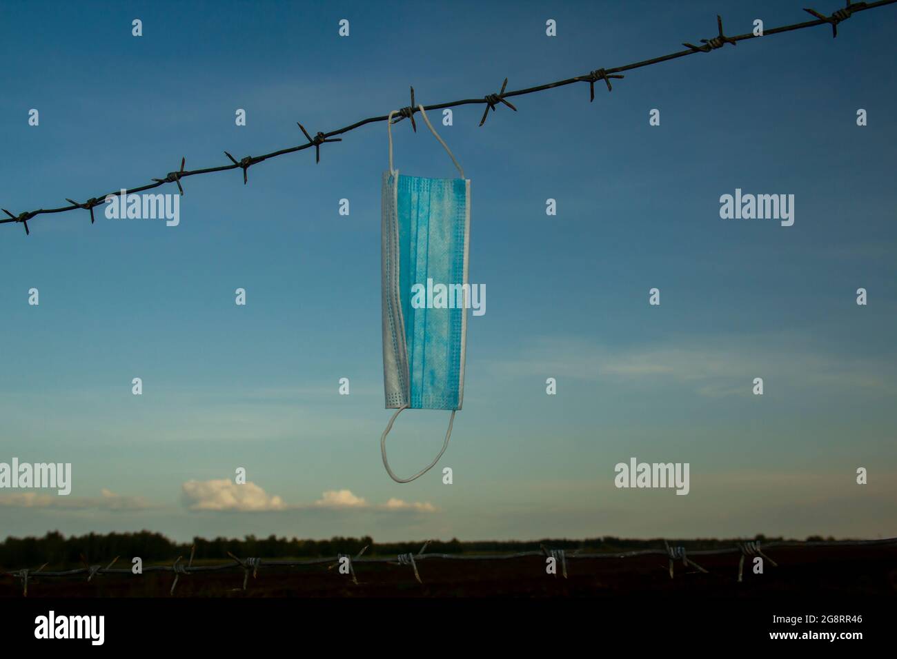 Medical mask hanging on a barbed wire against the sky. The concept of ...