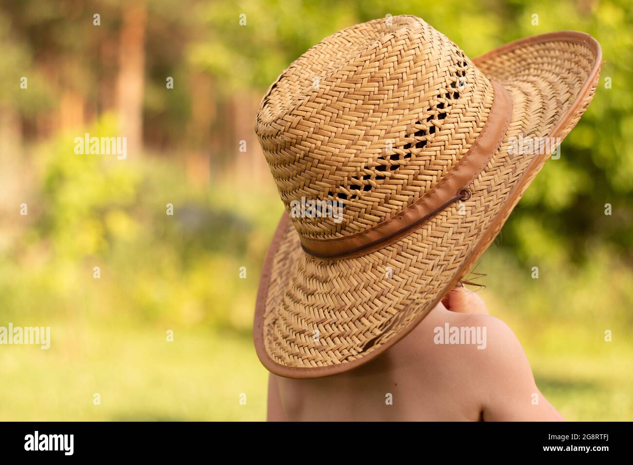 A small lovely child in a straw farm hat looks into the distance with ...