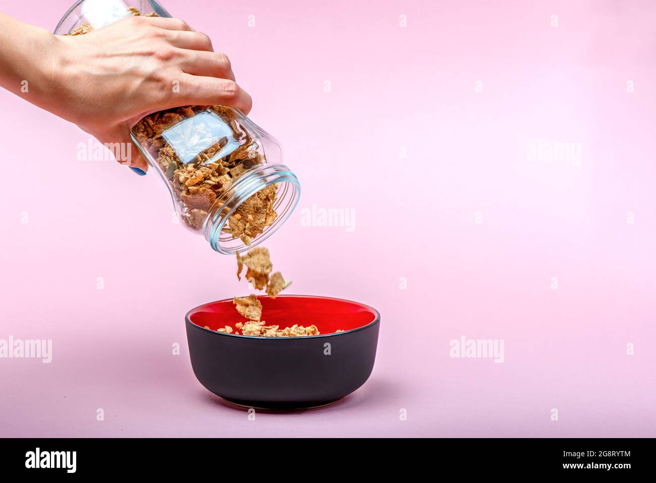 Muesli on a pink background. Pour dry muesli flakes by hand into a bowl ...