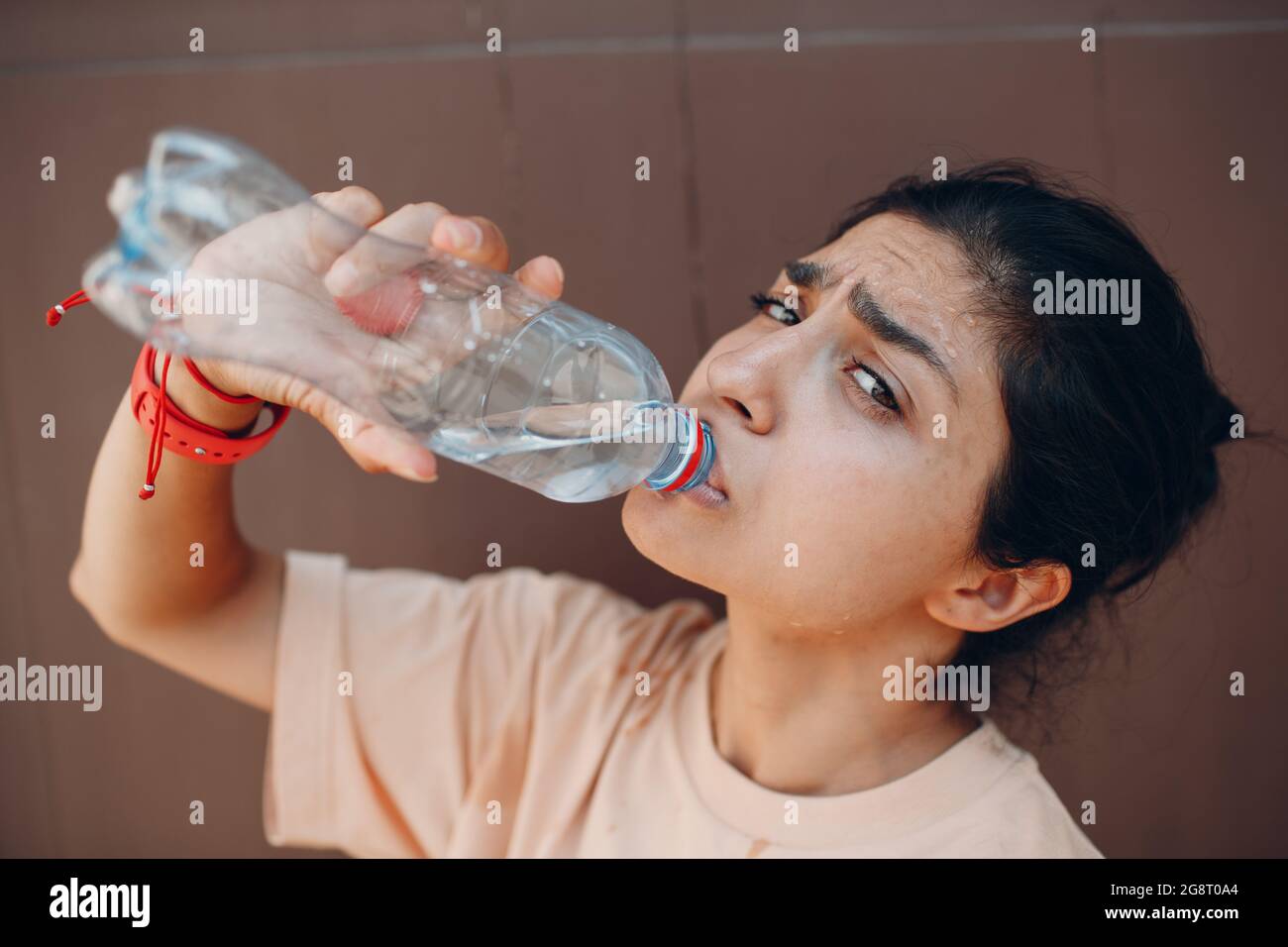 Indian woman drinking bottled still water outdoor wall. Sweat drops on ...