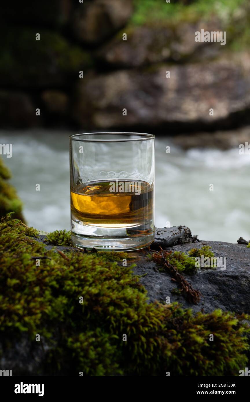 Glass of strong scotch single malt whisky with fast flowing mountain ...