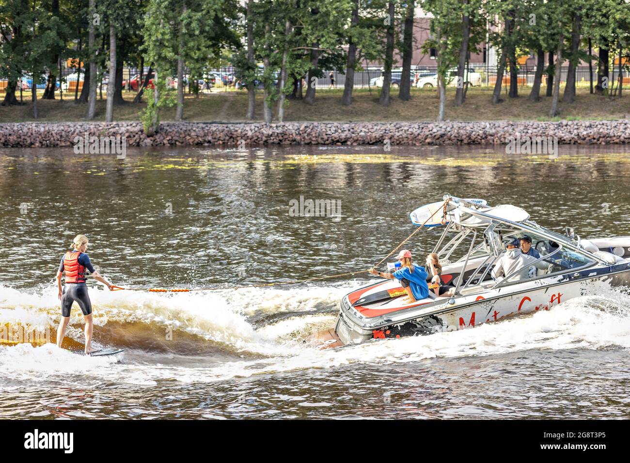 A young woman rides on a water board attached to a boat on the river ...