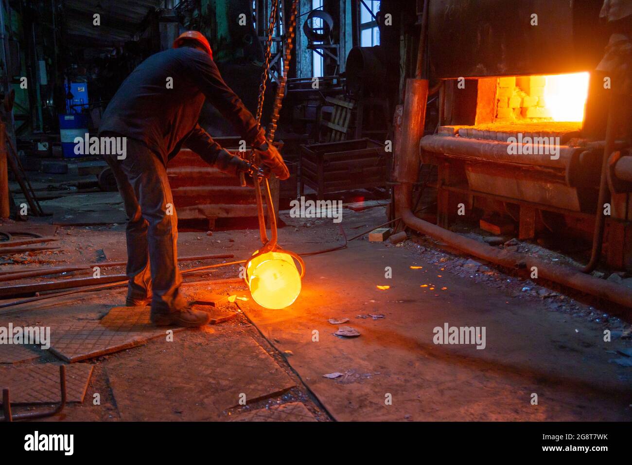 forge factory worker moving glowing hot metal workpiece with chain ...
