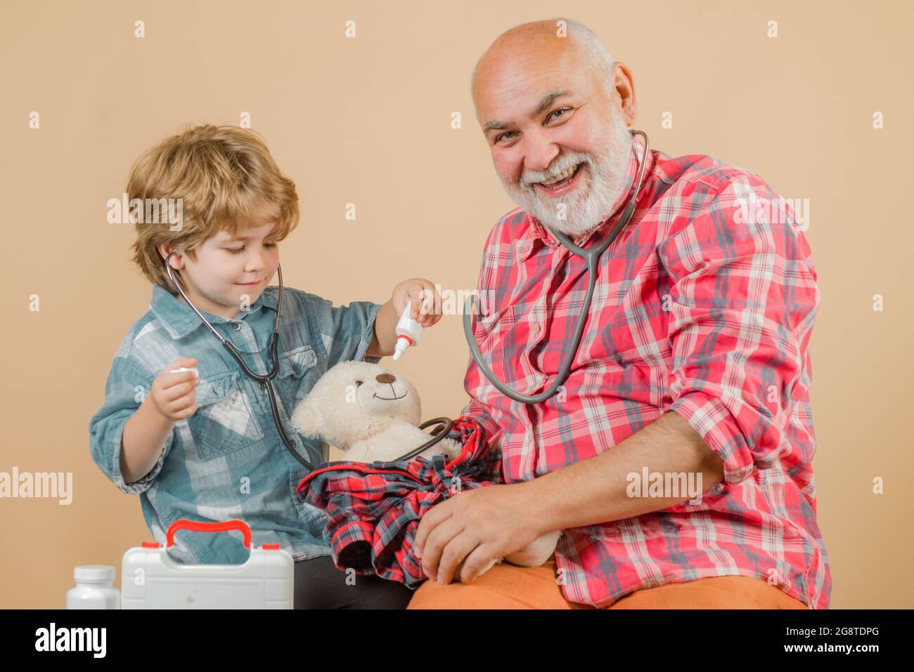 Little doctor. Charming little boy examining a cheek of his grandfather ...