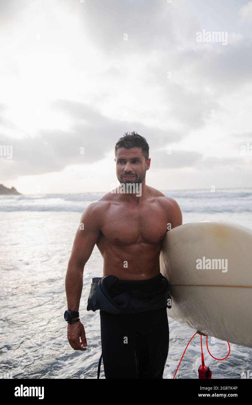 Male surfer holding surf board at the beach at sunset, he is young ...