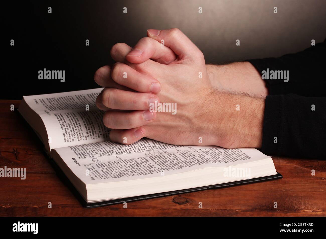Hands folded in prayer over a Holy bible on wooden table on grey ...