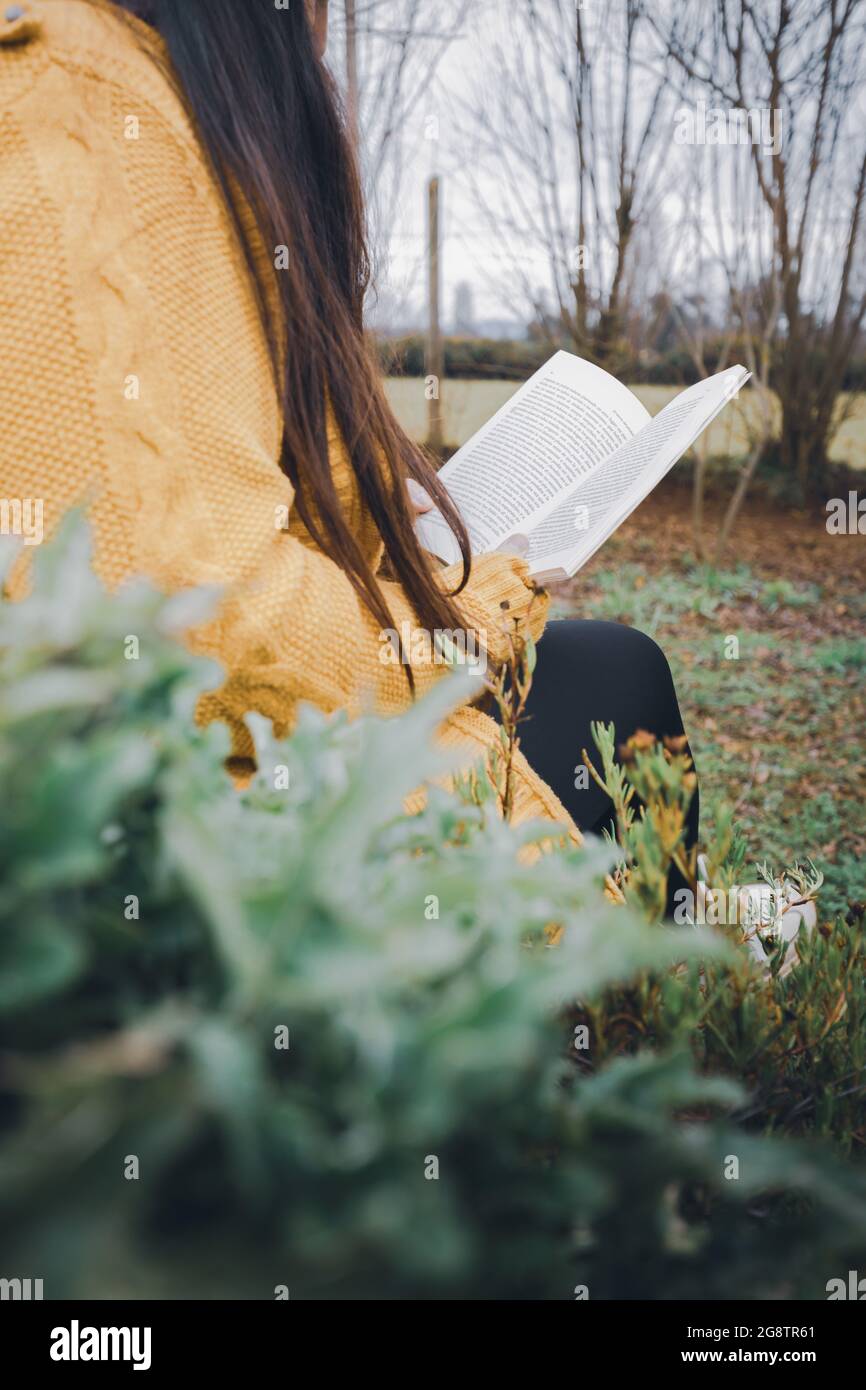 Young woman sitting outdoor and reading a book Stock Photo - Alamy