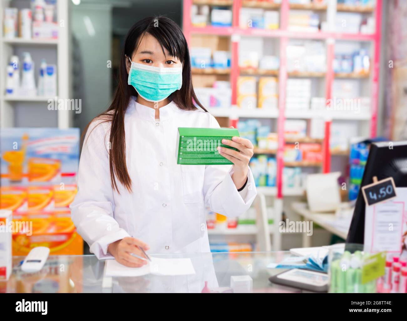 Chinese female pharmacist in protective facial mask standing among ...