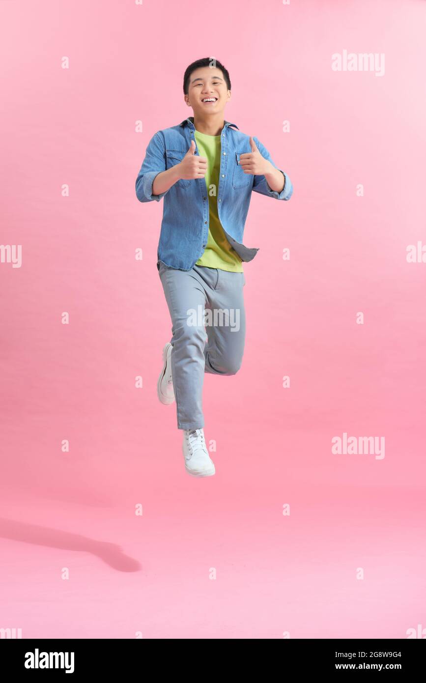 Energetic happy young Asian man jumping isolated in pink background ...