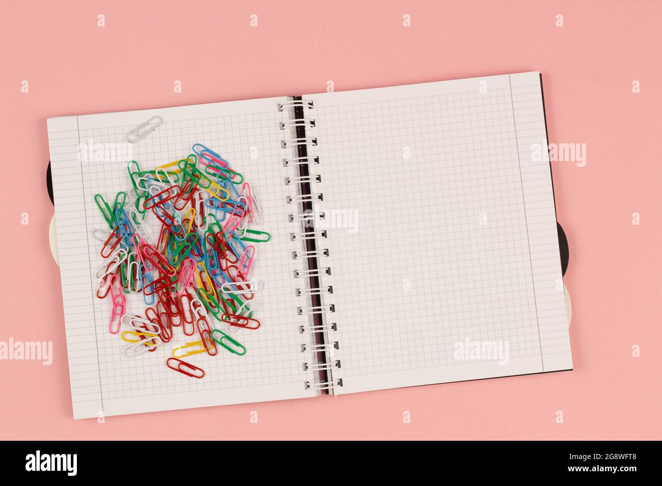 Open school squared notebook and colorful clips on the pink background ...