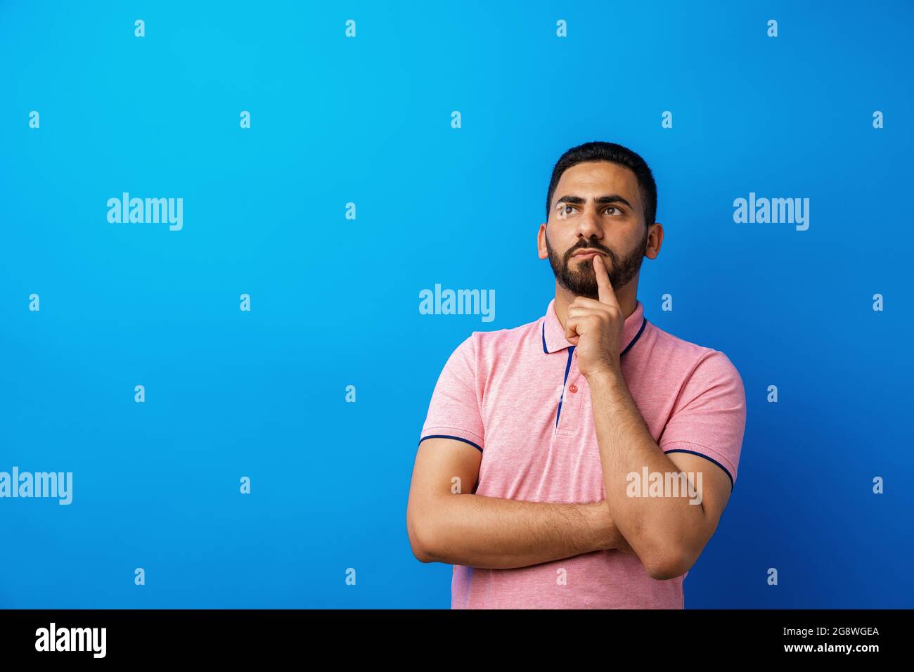 Pensive young arab man thinking and looking up against blue background ...