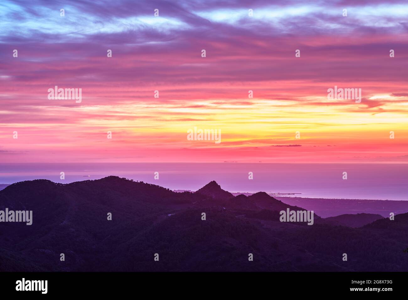 Vibrant warm sunrise over calm sea and mountain landscape in La Plana ...