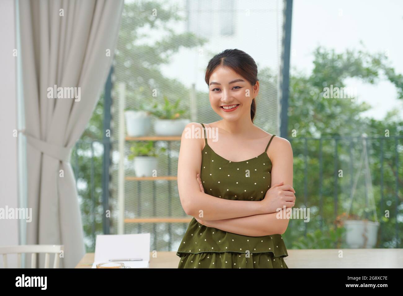 Smiling pretty young adult woman looking at camera posing at modern home arms crossed Stock ...