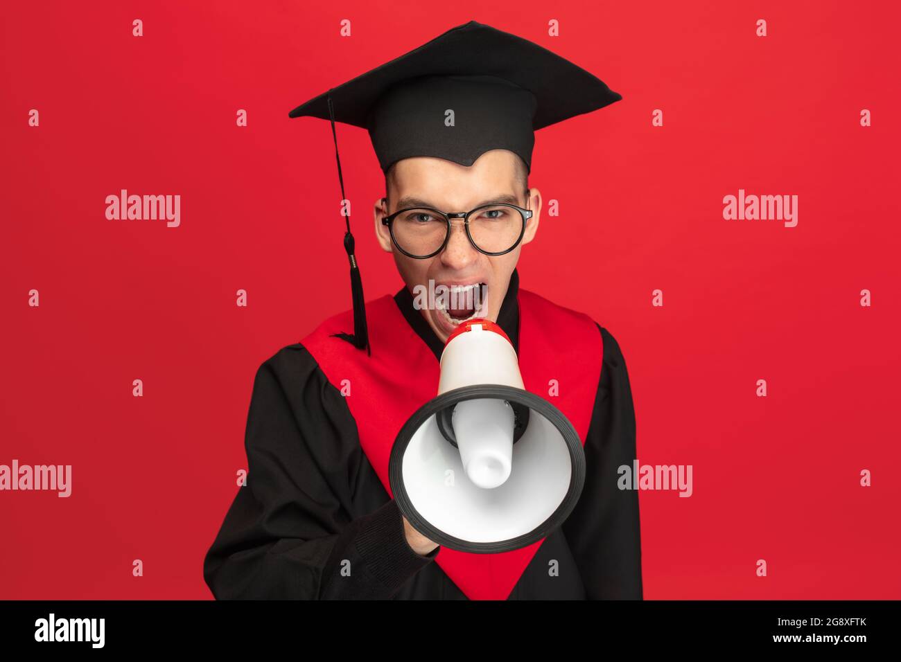 Portrait of young student, graduate in mantle with megaphone isolated ...