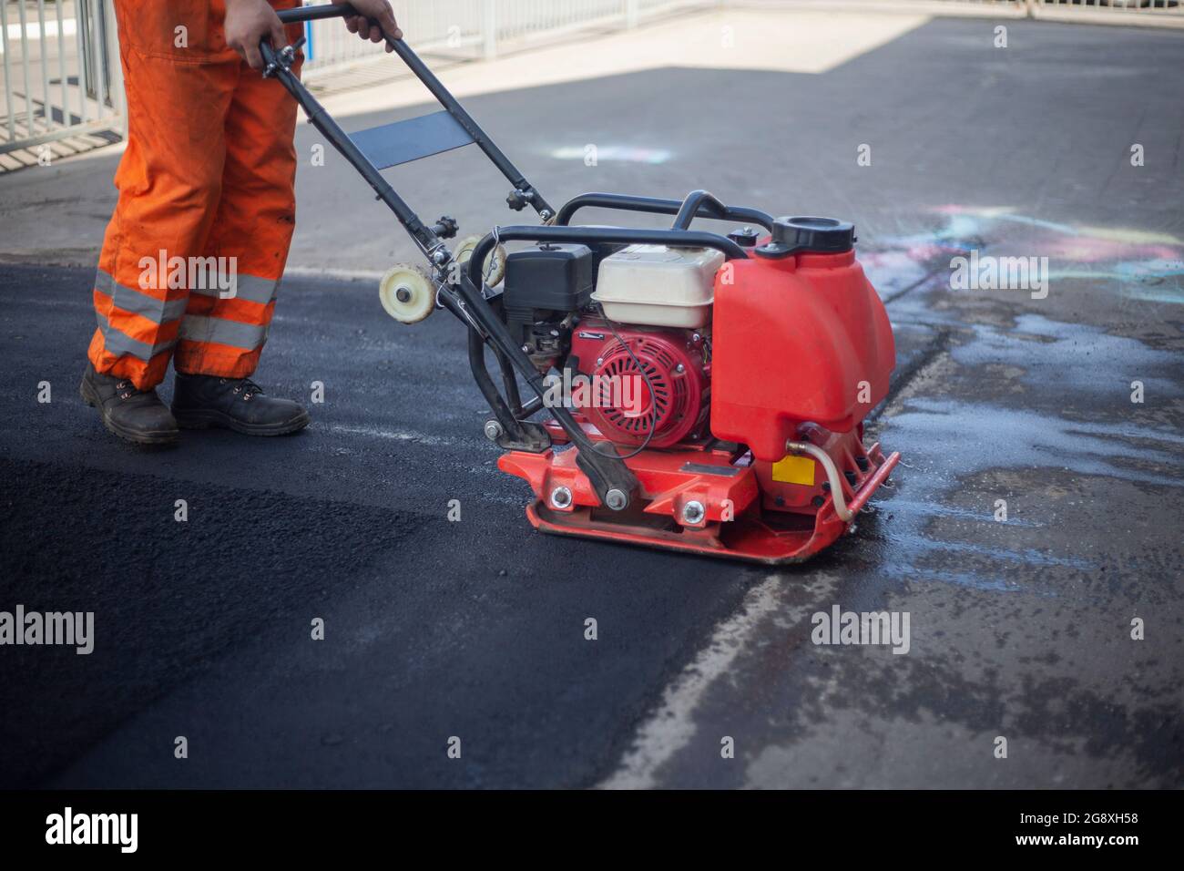 Asphalt laying. Leveling the road. A worker compresses warm asphalt ...