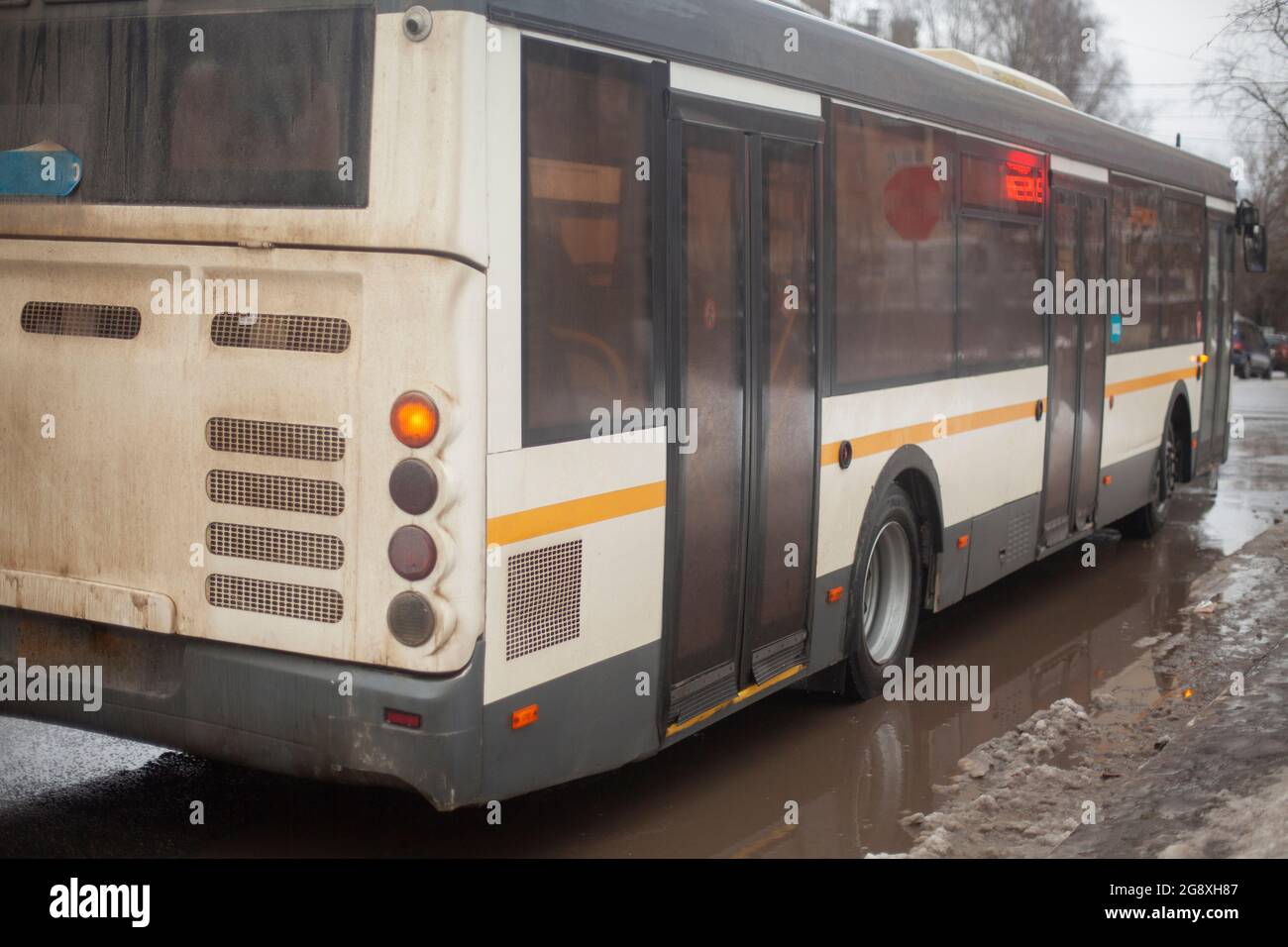 Bus in winter. Transport on the road travels through a puddle. Regular ...