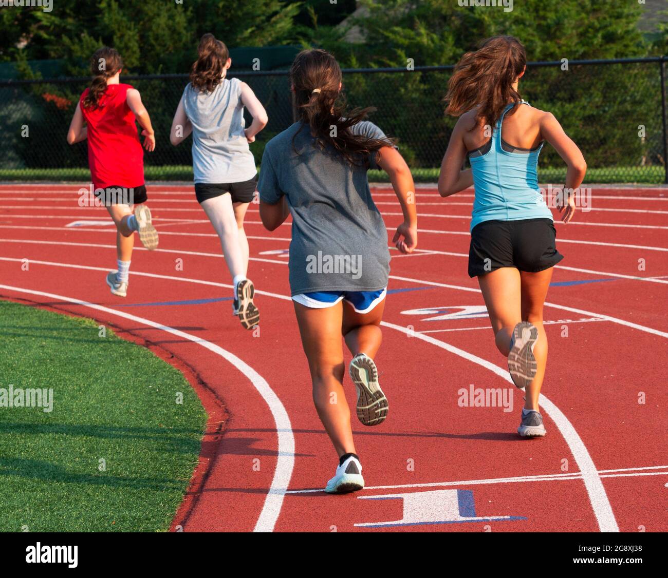 Rear View Of A Group Of High School Girls Running Fast On A Track During Summer Camp Workouts