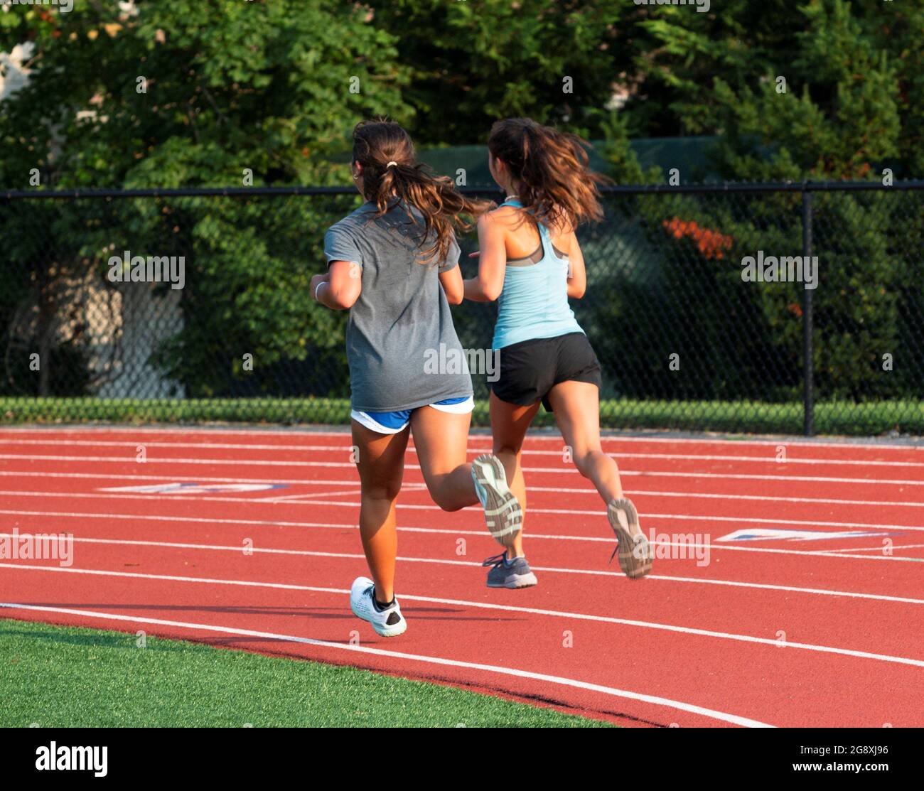 Rear view of two high school girls running together on the first turn ...