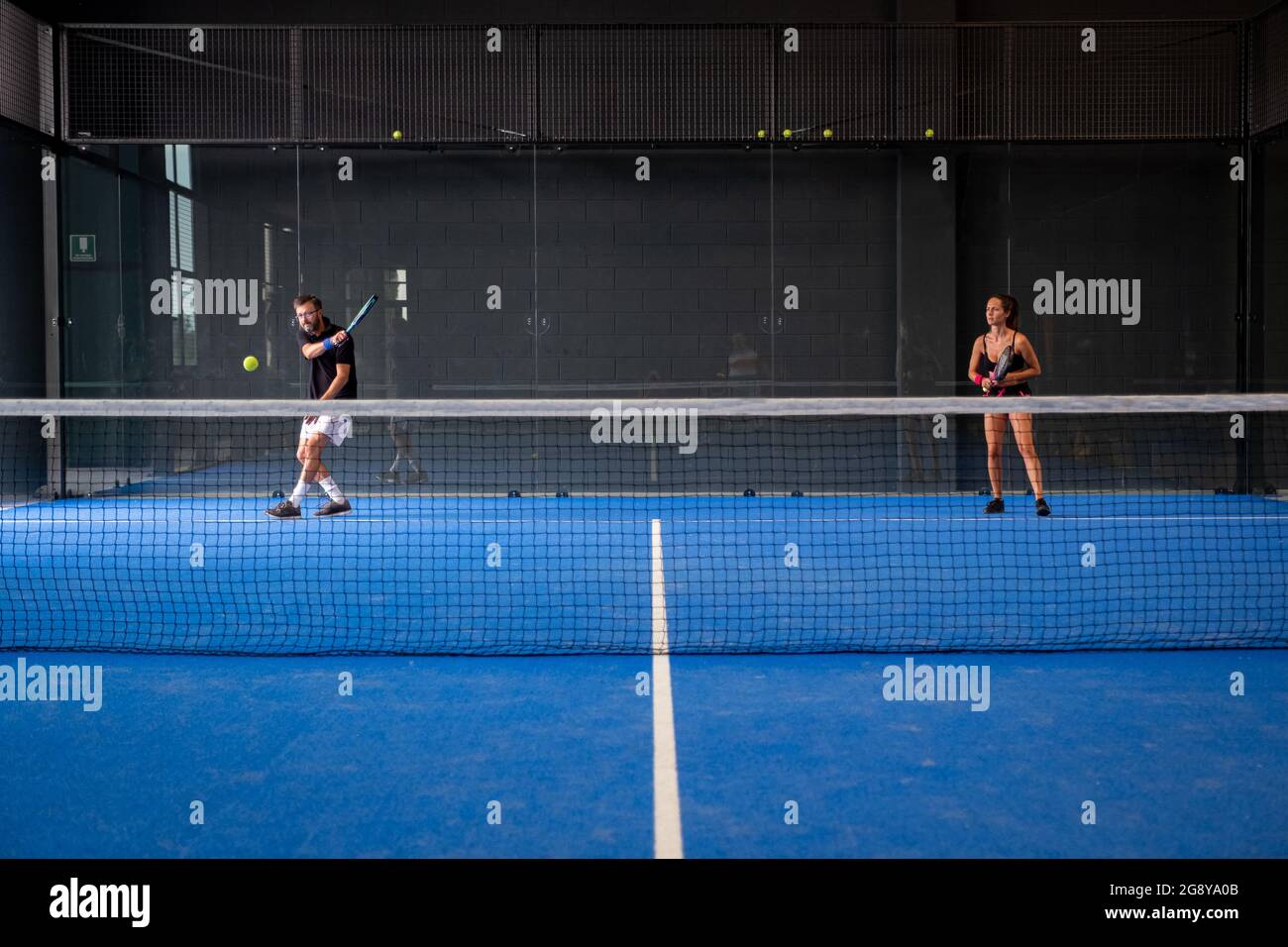 Mixed padel match in a blue grass padel court indoor behind the net ...
