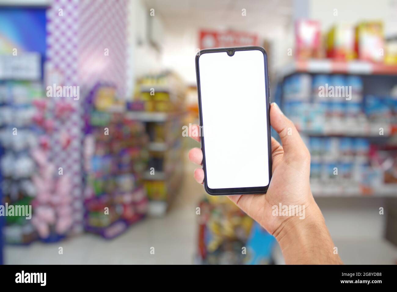 Hand holding smartphone with blank white screen, blurry supermarket ...