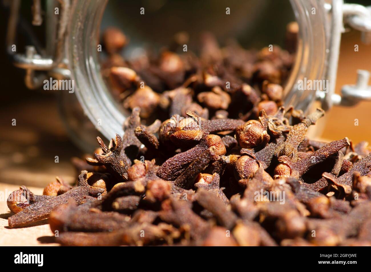 Closeup of dried clove seeds in a jar on a wooden surface with a blurry ...