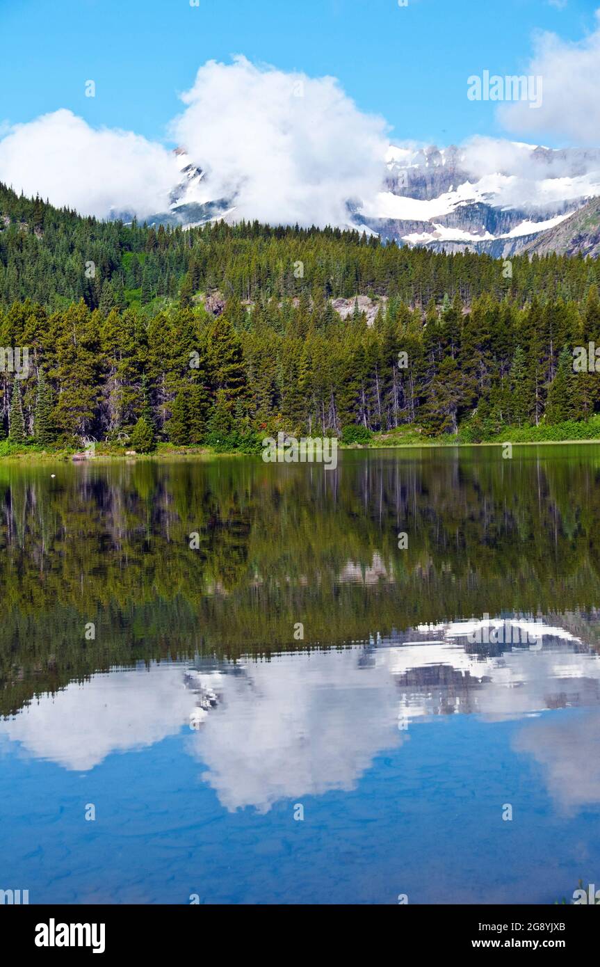 Mountains and clouds reflected in still water of Fishercap Lake ...