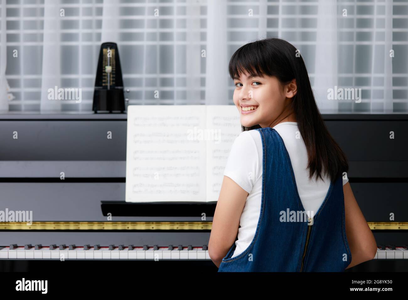 Young pretty beautiful Asian girl sitting at piano with blur music ...