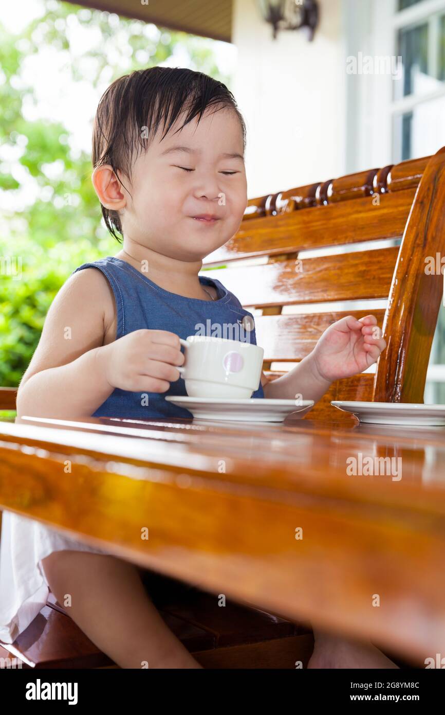 Little asian girl smiling and holding a teacup at home exterior in ...
