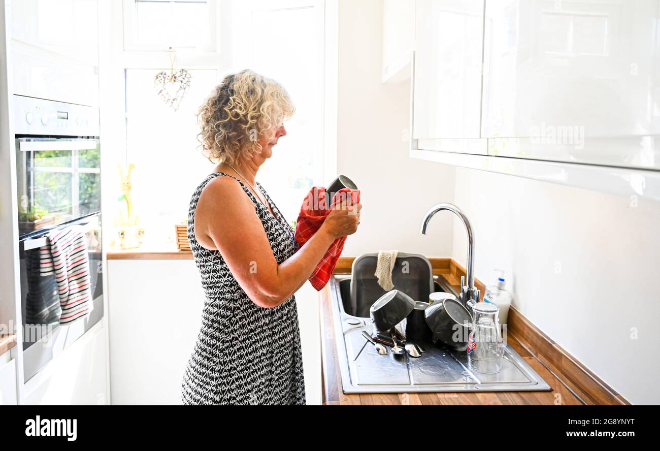Woman doing up dishes in brightly lit kitchen in daylight household ...