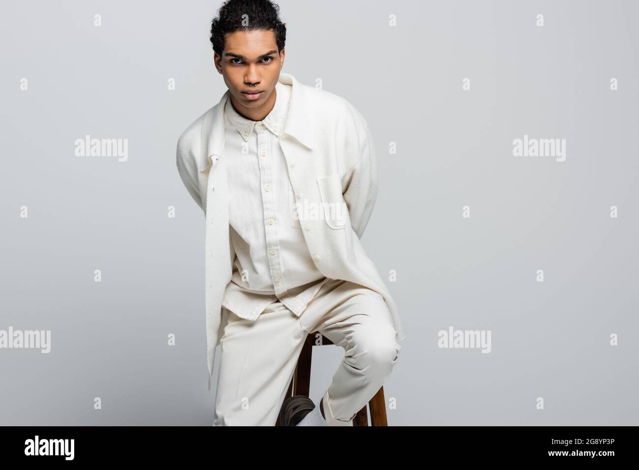 trendy african american guy in white suit posing on stool with hands ...