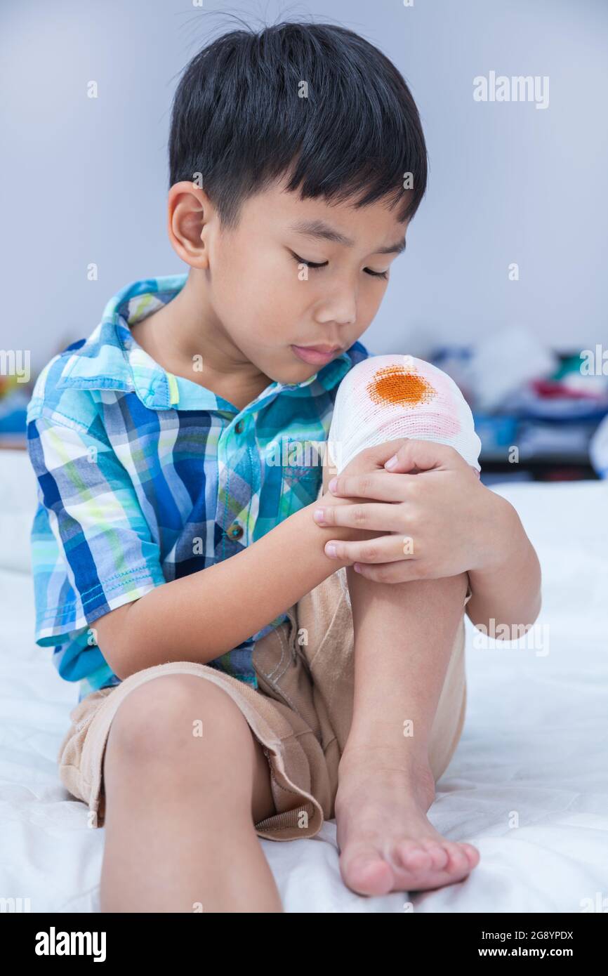 Child injured. Asian handsome boy looking at wound on his knee with ...