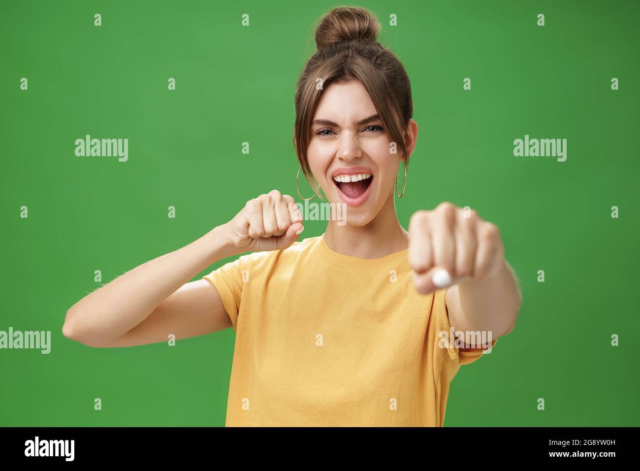 Cute female rebel in yellow t-shirt with gap teeth pulling fist towards ...