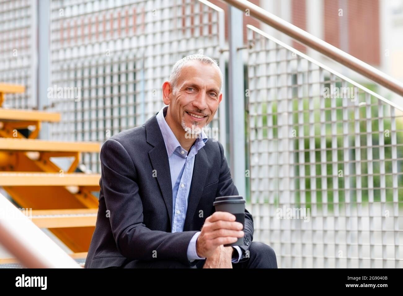Smiling businessman holding reusable cup while sitting on steps Stock ...