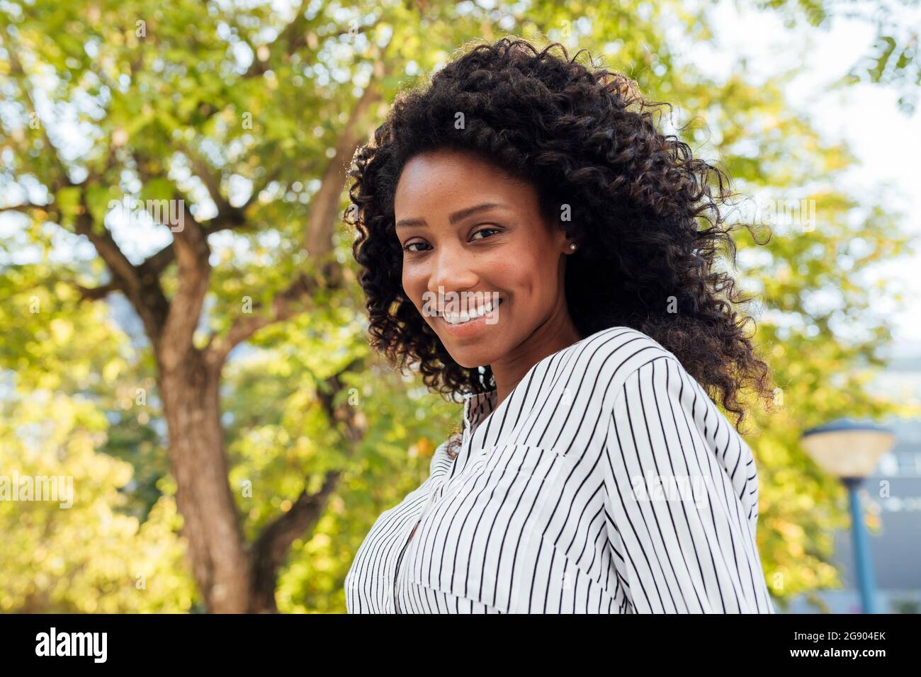 Smiling beautiful woman with curly hair standing at park Stock Photo ...