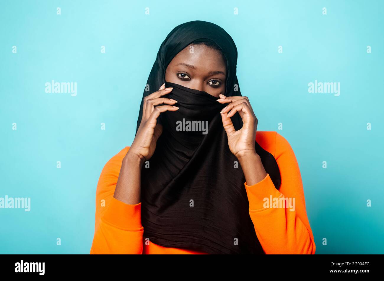 Woman covering face with hijab in front of blue background Stock Photo ...