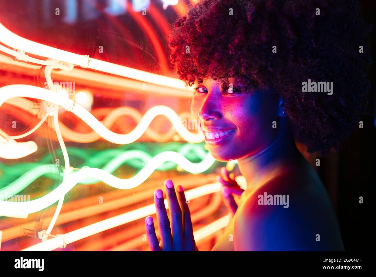 Smiling Afro woman touching neon lights Stock Photo - Alamy