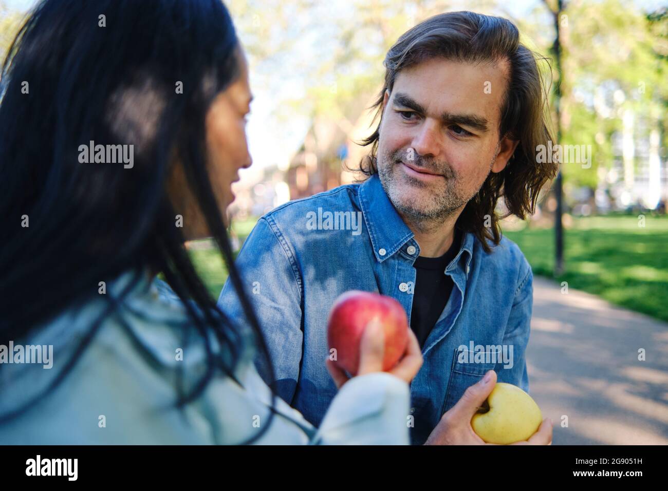 Mature man looking at wife having apple in park Stock Photo - Alamy