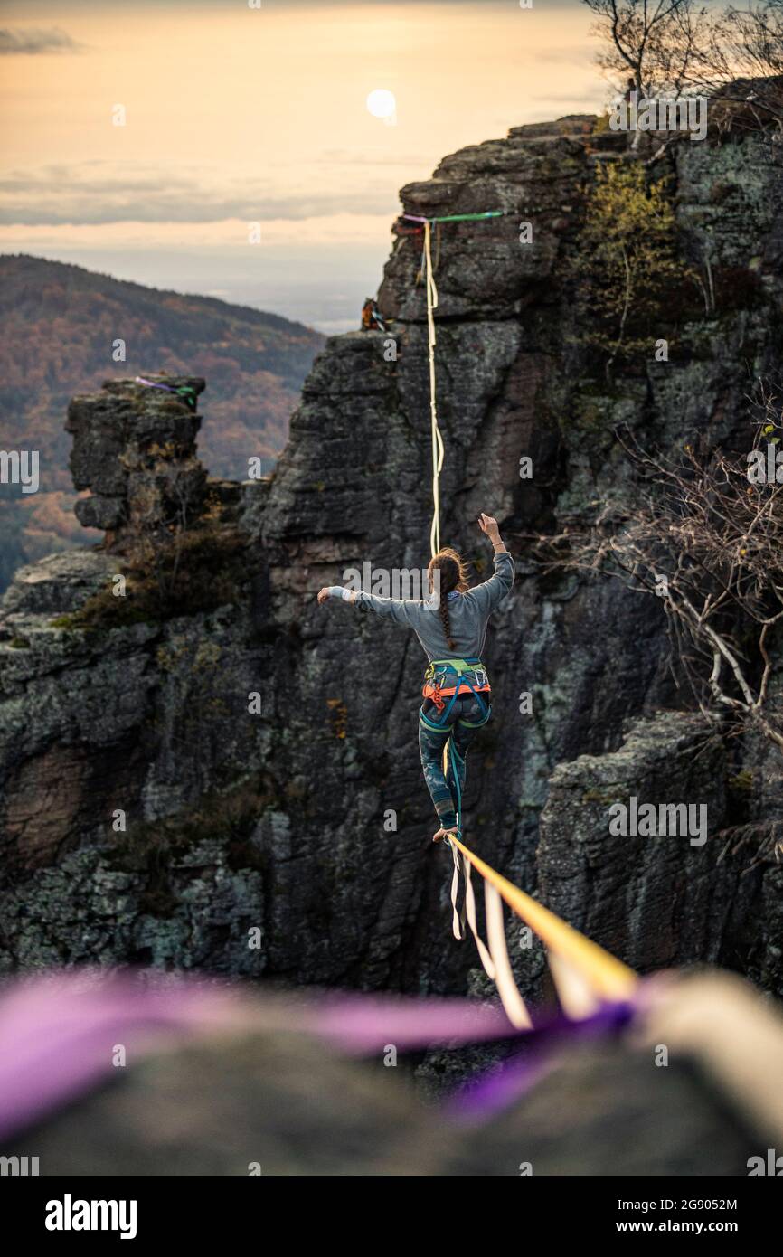 Mid adult woman balancing while highlining in mountains during sunset ...
