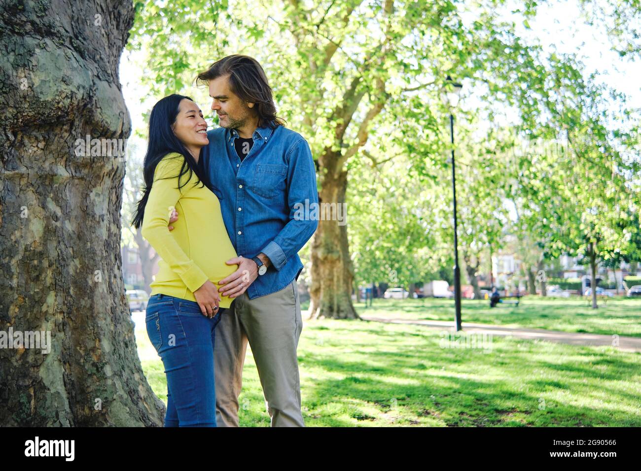 Smiling pregnant woman looking at husband by tree trunk Stock Photo - Alamy