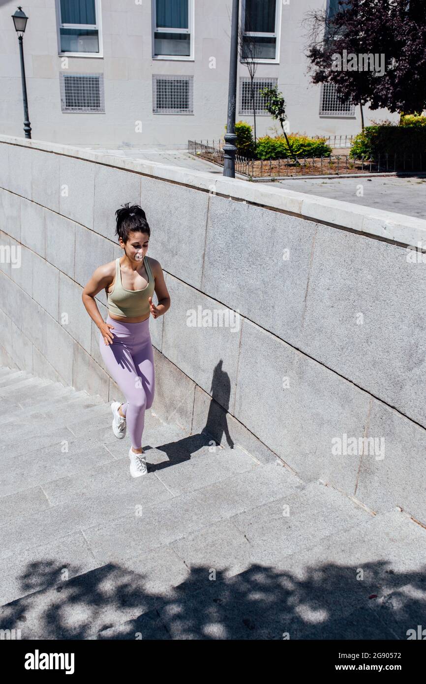 Young female athlete running on steps by surrounding wall Stock Photo ...