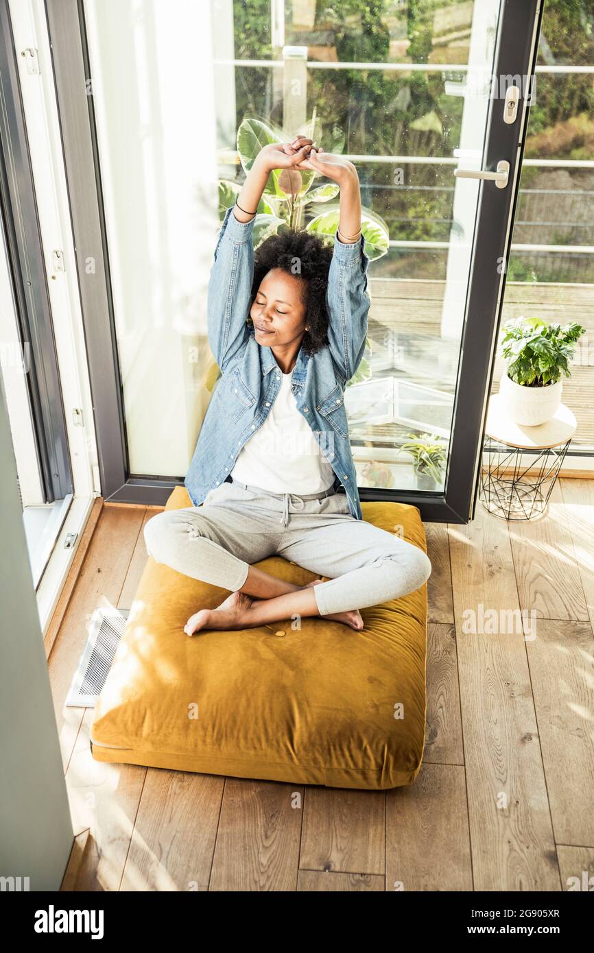 Woman stretching hands while sitting on cushion at home Stock Photo - Alamy