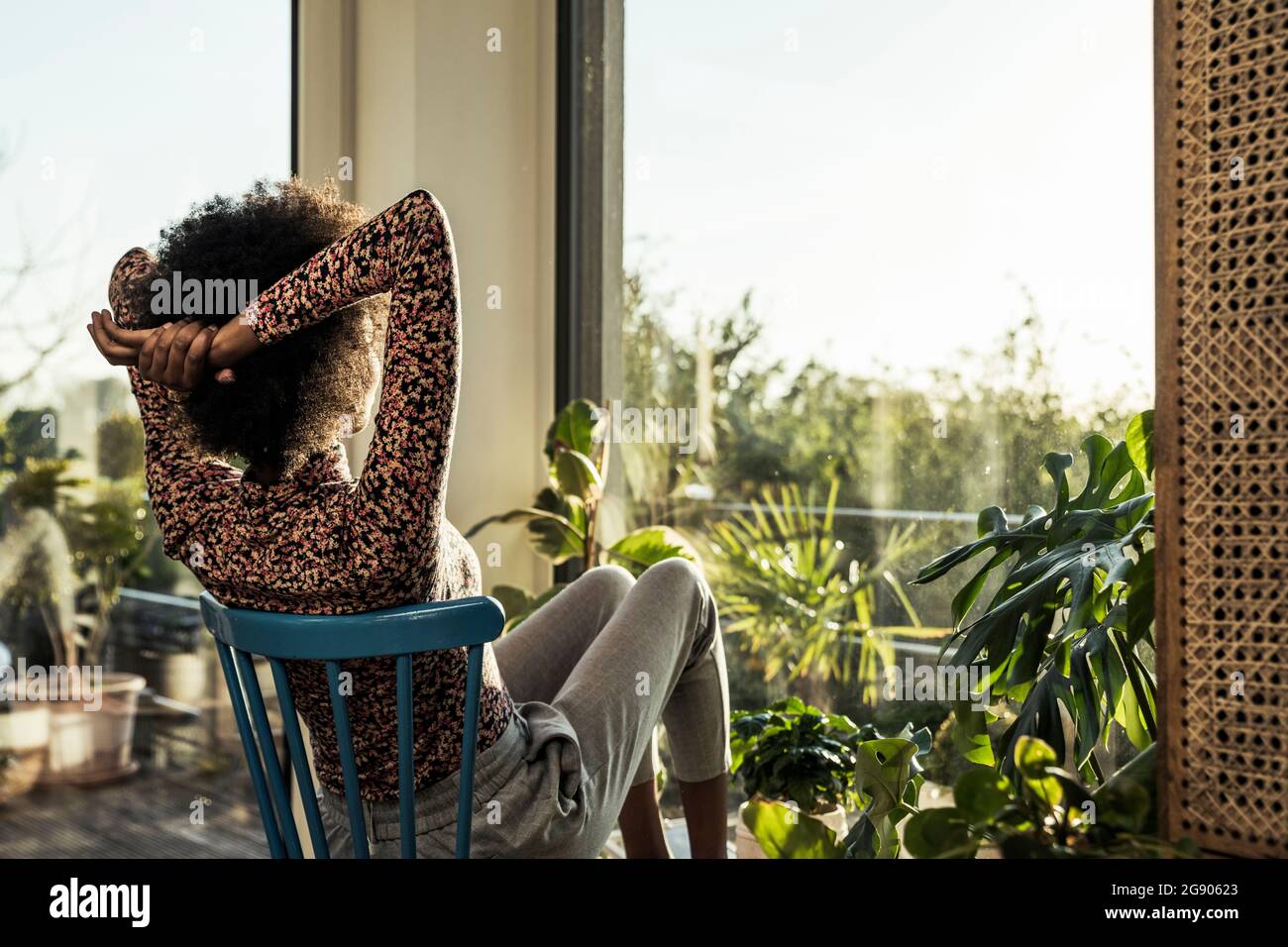 Young woman with hands behind head sitting on chair at home Stock Photo ...