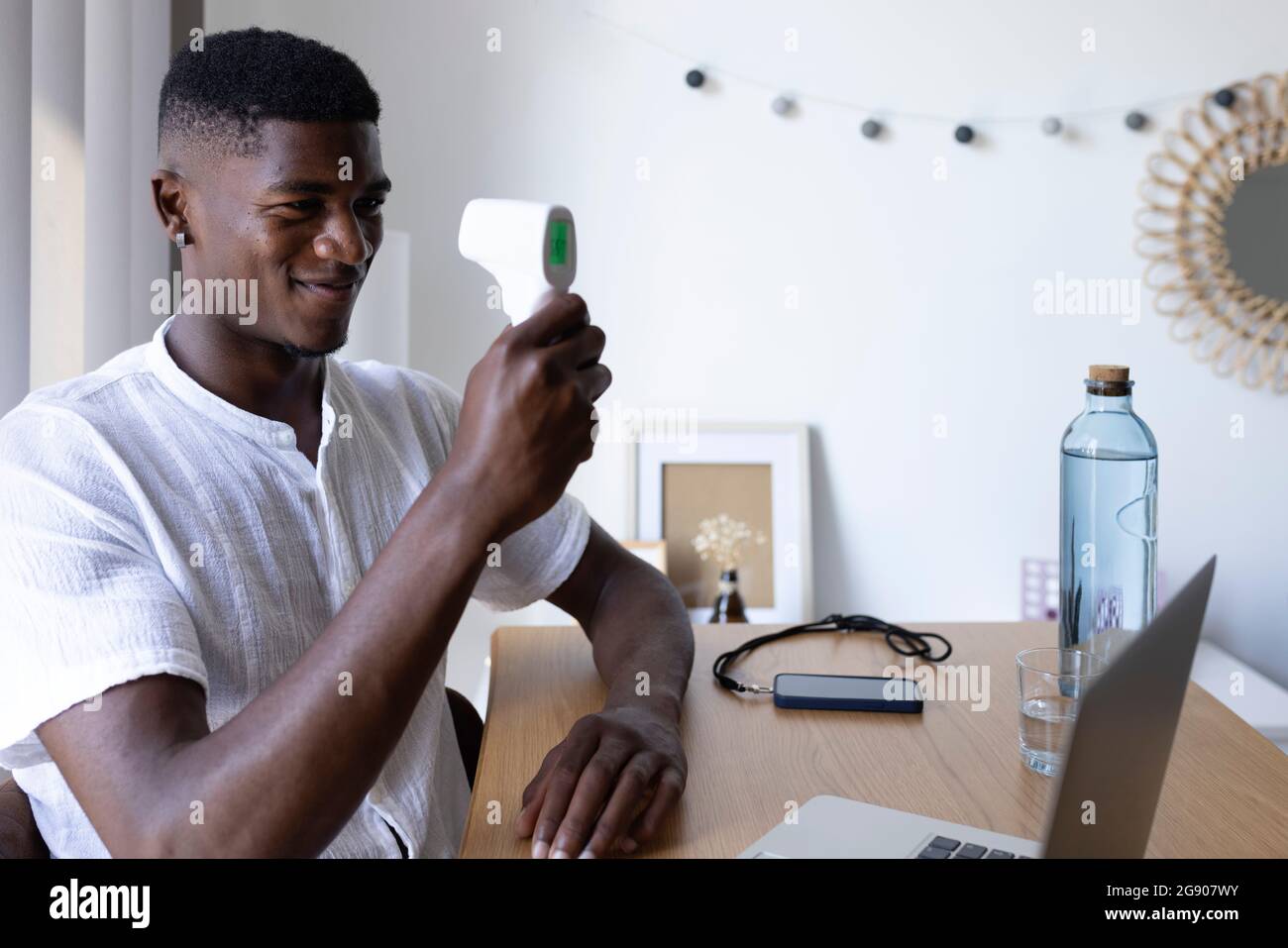 Smiling man checking temperature through infrared thermometer at home ...