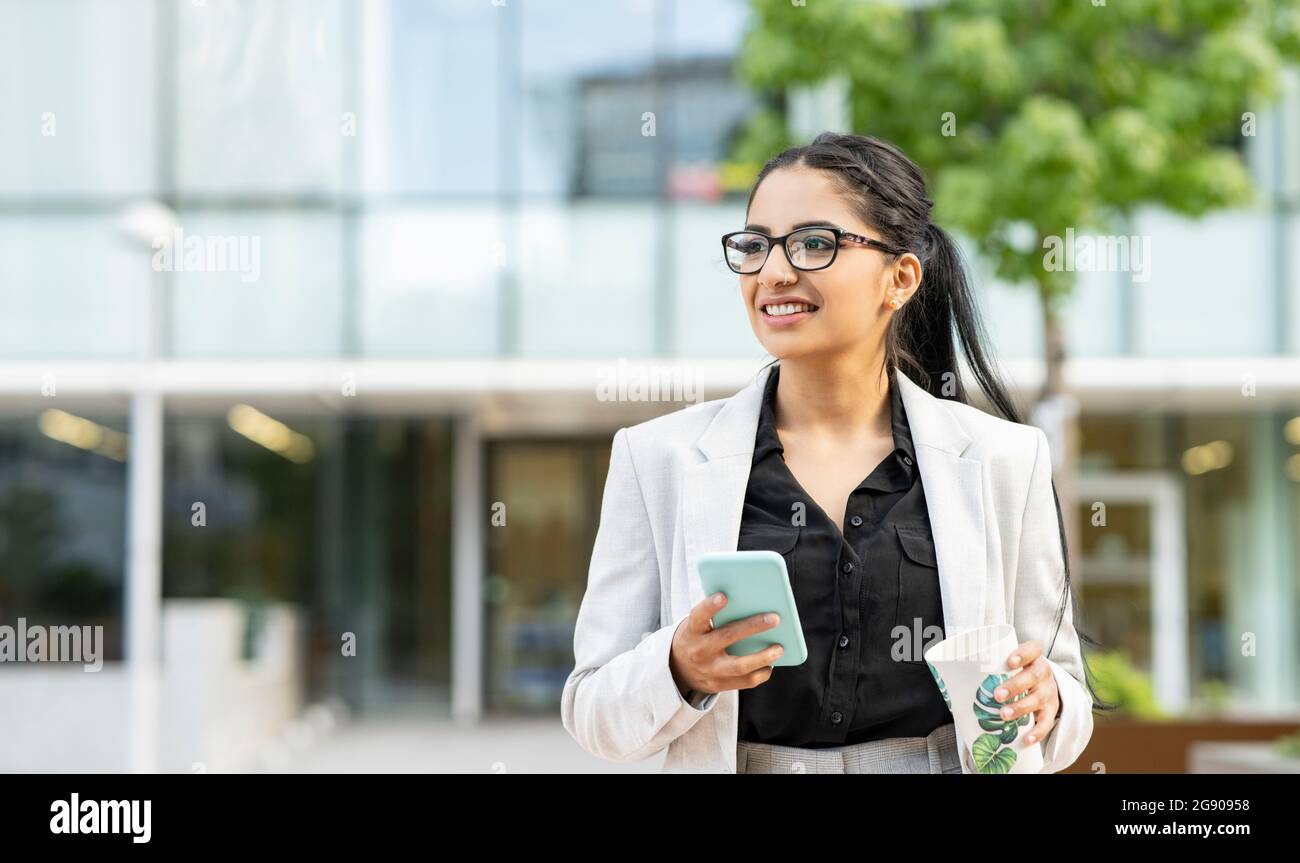 Female professional with disposable cup talking on mobile phone in city ...